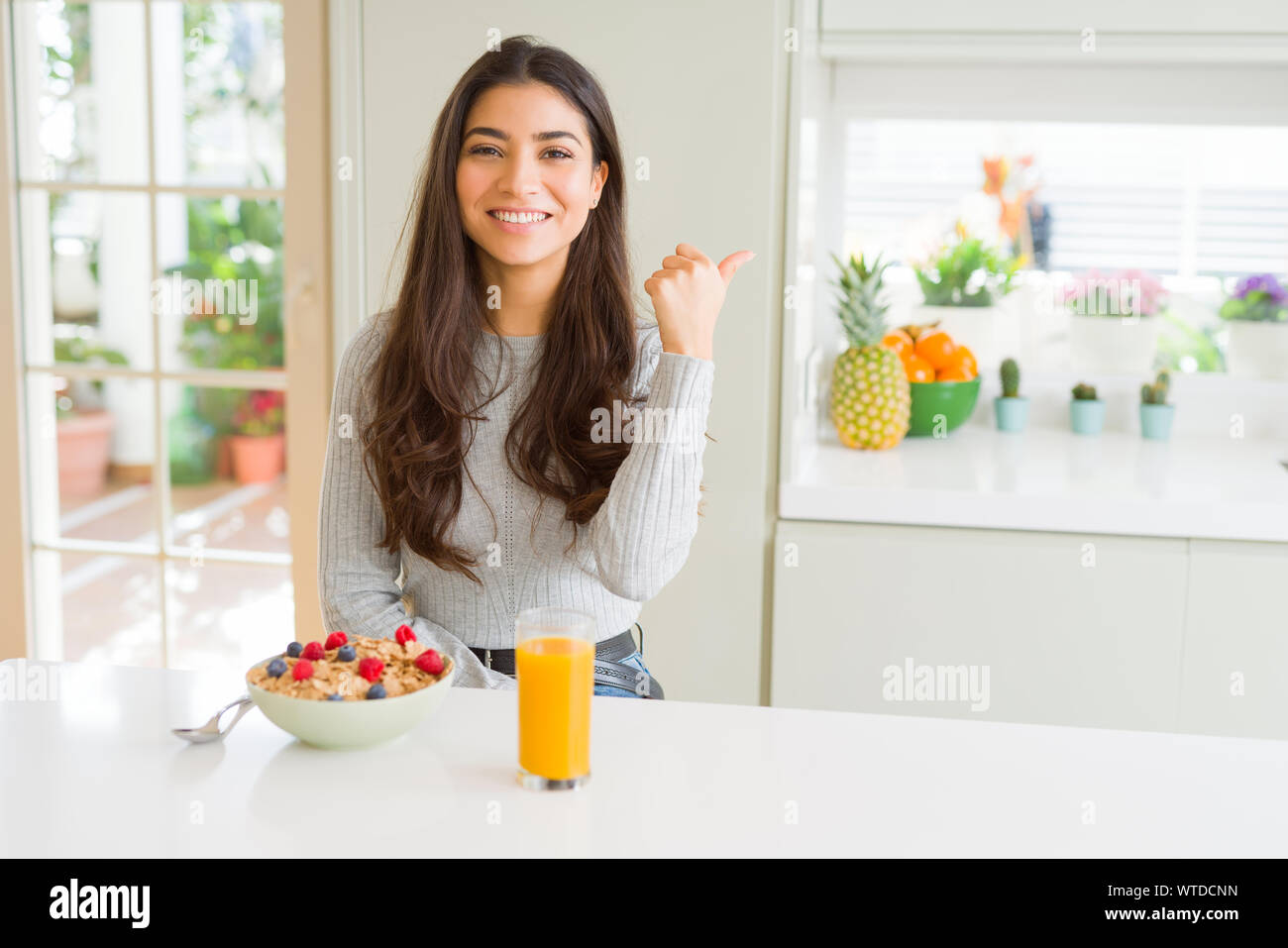 Young woman eating healthy breakfast in the morning smiling with happy face looking and pointing ...
