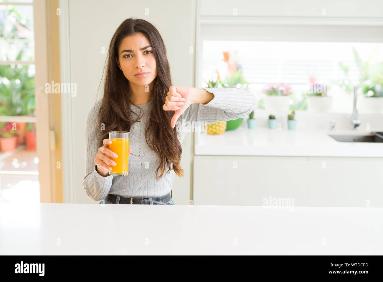 Young woman drinking a glass of fresh orange juice with angry face ...
