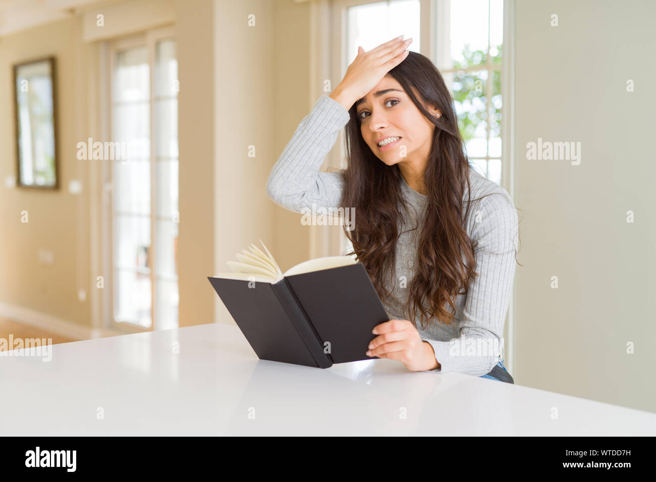 Young woman reading a book stressed with hand on head, shocked with ...