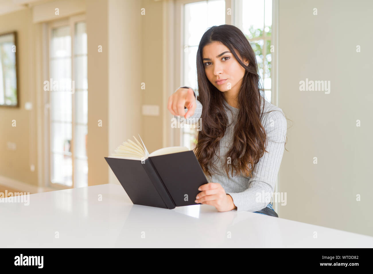 Young woman reading a book pointing with finger to the camera and to ...