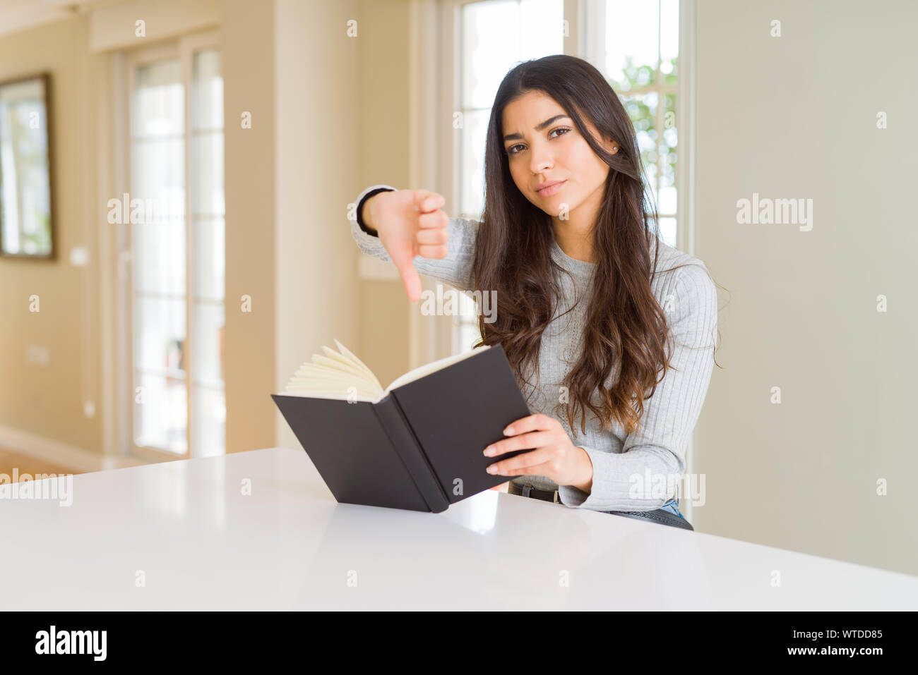 Young woman reading a book with angry face, negative sign showing ...