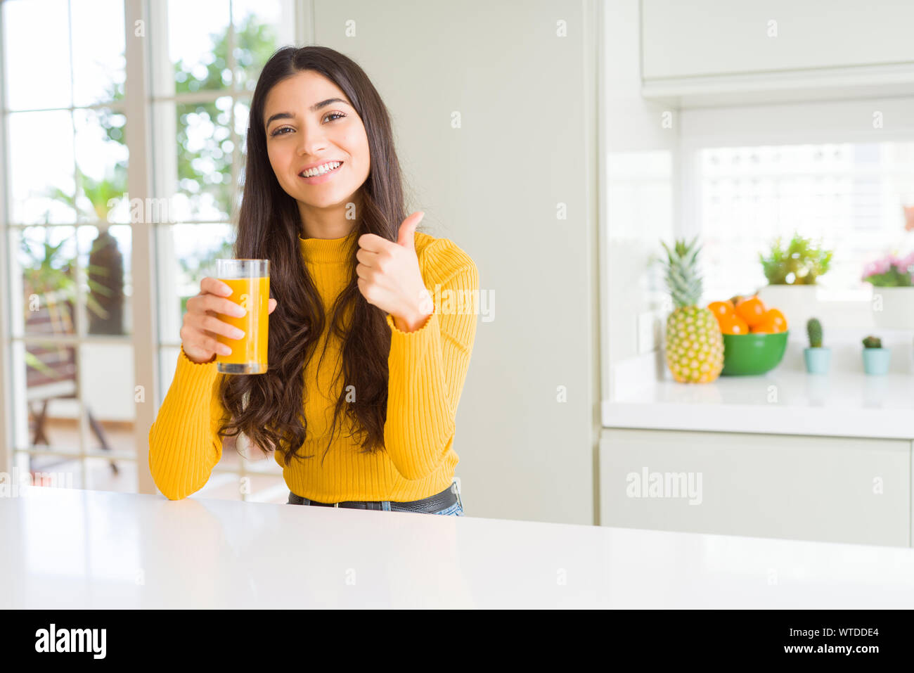 Young woman drinking a glass of fresh orange juice happy with big smile ...