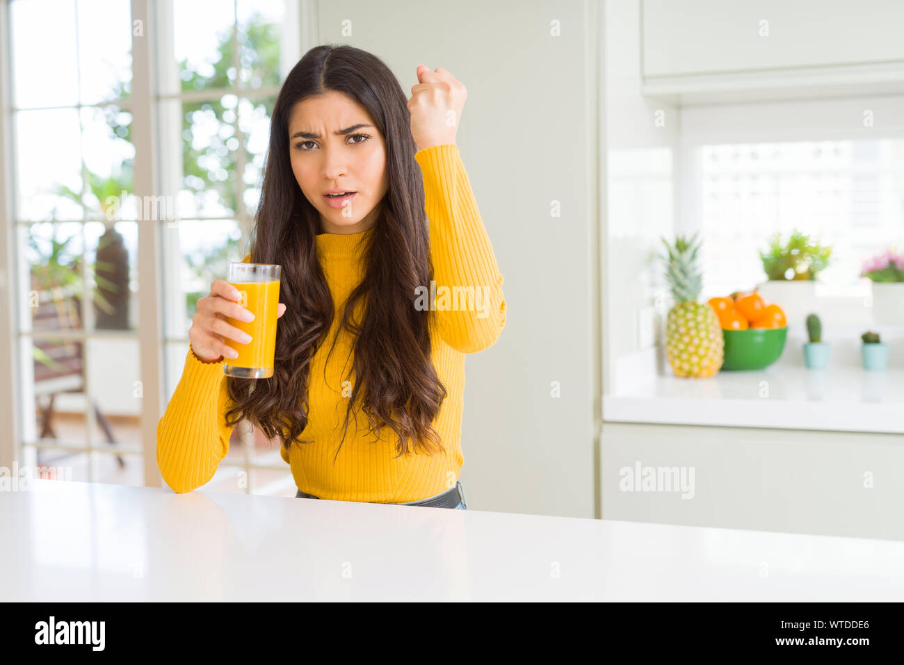 Young woman drinking a glass of fresh orange juice annoyed and ...