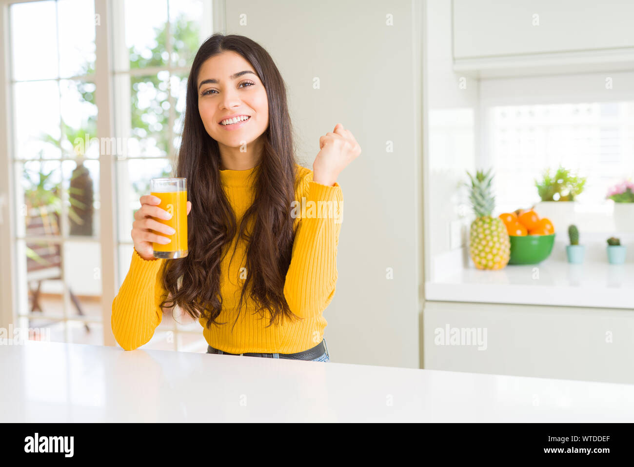 Young woman drinking a glass of fresh orange juice screaming proud and ...