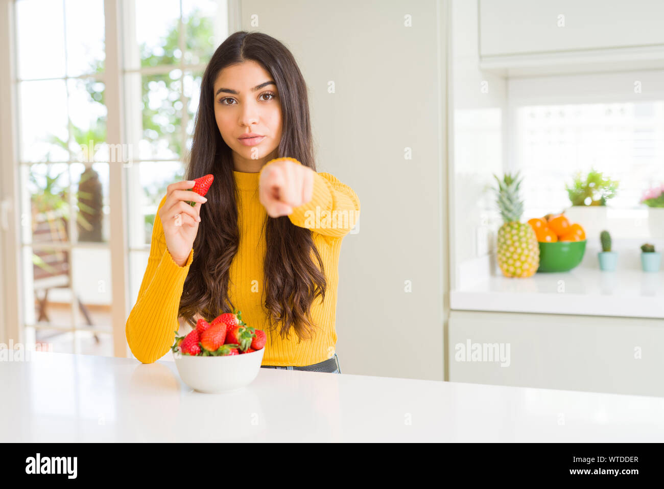 Young woman eating fresh red strawberry as healthy snack pointing with ...