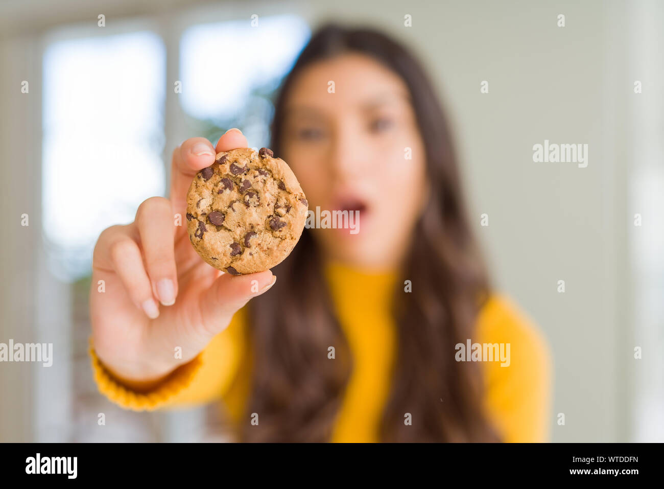Young woman eating chocolate chips cookies at home scared in shock with ...