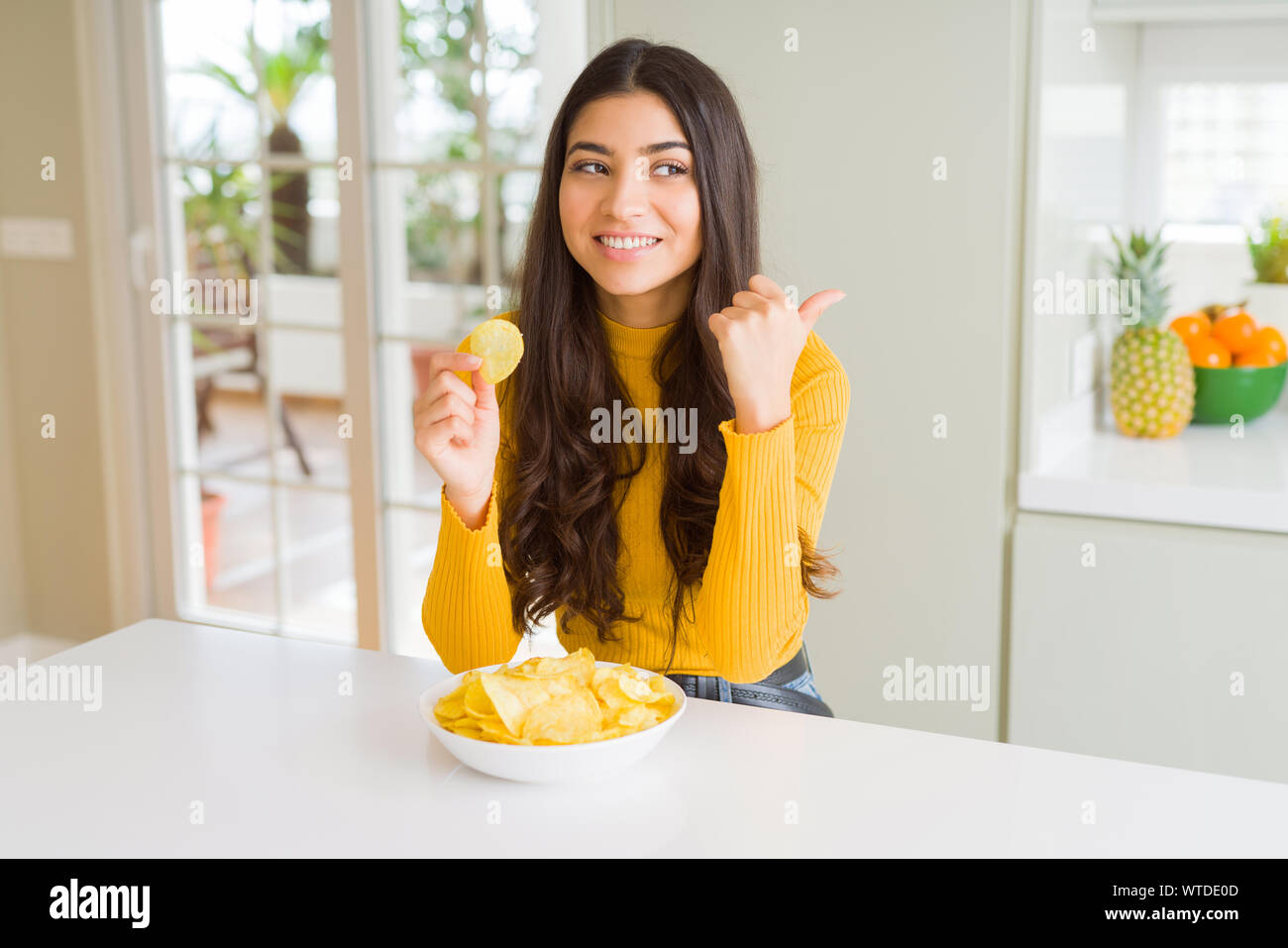 Young woman eating fastfood potato chips pointing and showing with ...