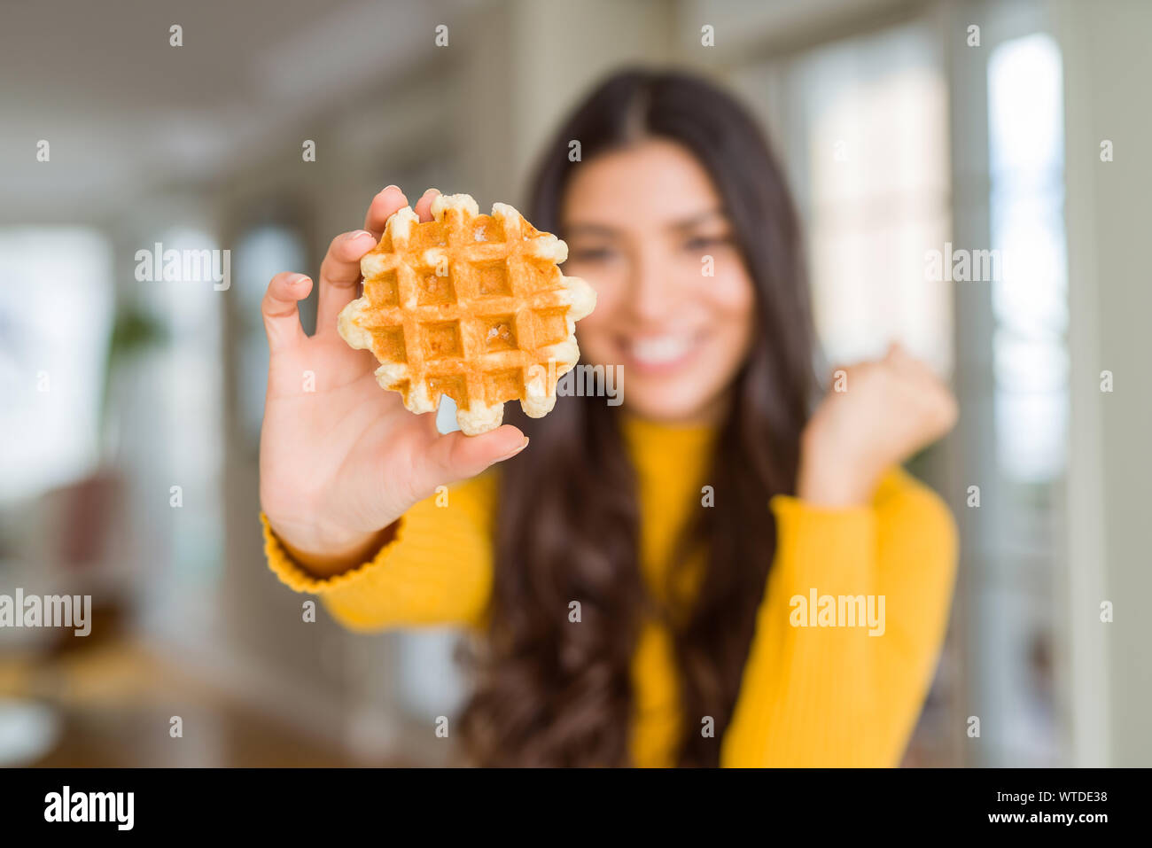 Young woman eating sweet waffle pastry screaming proud and celebrating ...