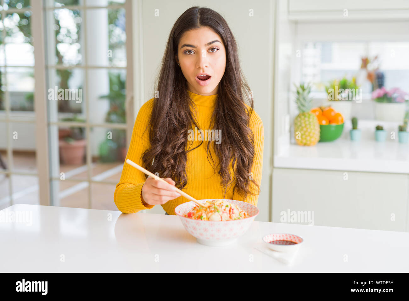 Young woman eating a bowl of Asian rice using chopsticks scared in ...