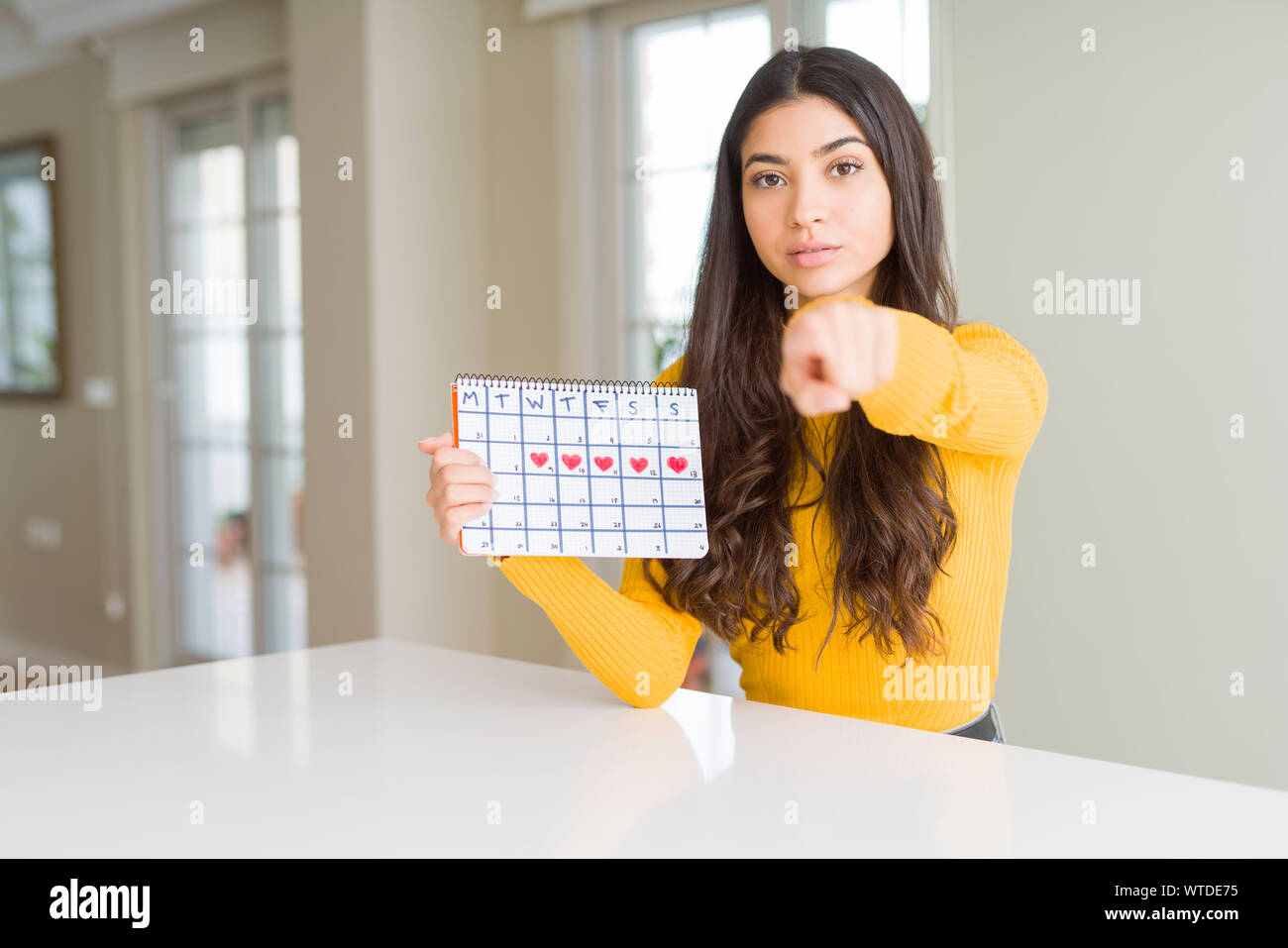 Young woman holding menstruation calendar pointing with finger to the ...