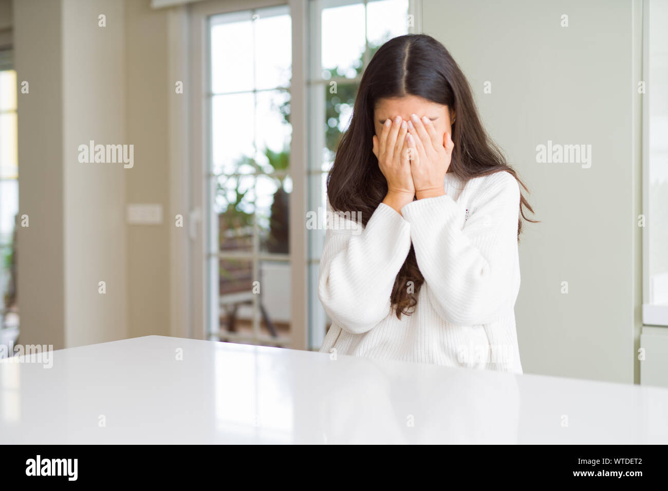 Young beautiful woman at home on white table with sad expression ...
