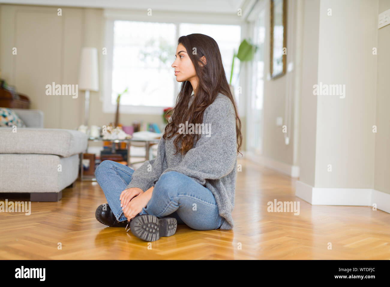 Young beautiful woman sitting on the floor at home looking to side ...
