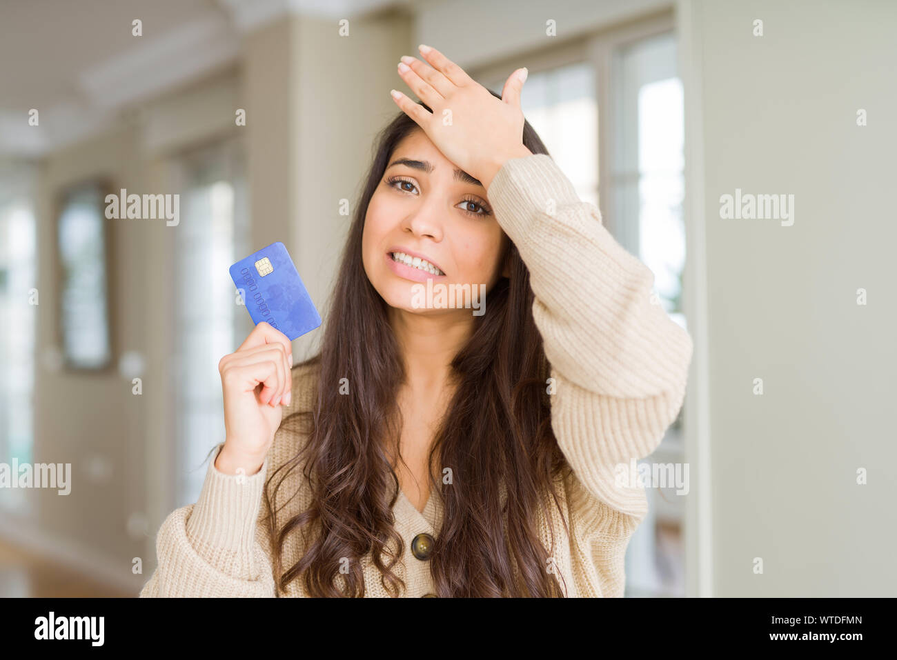 Young woman holding credit card as payment stressed with hand on head ...