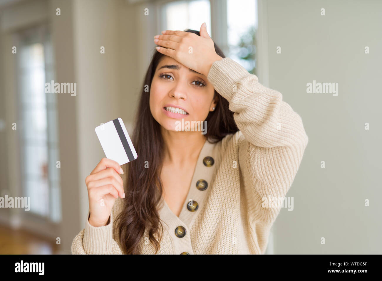 Young woman holding credit card as payment stressed with hand on head ...