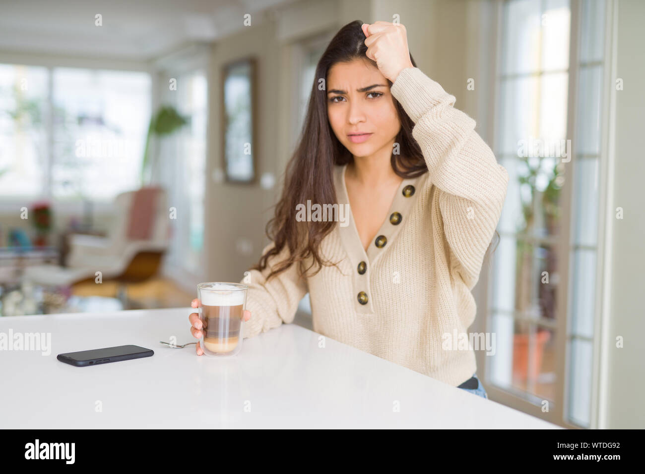 Young woman drinking a cup of coffee at home annoyed and frustrated ...