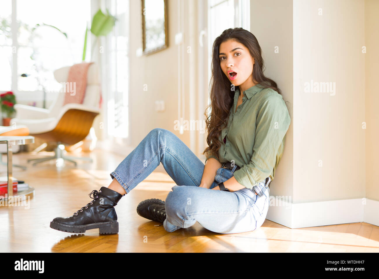 Young beautiful woman sitting on the floor at home afraid and shocked ...