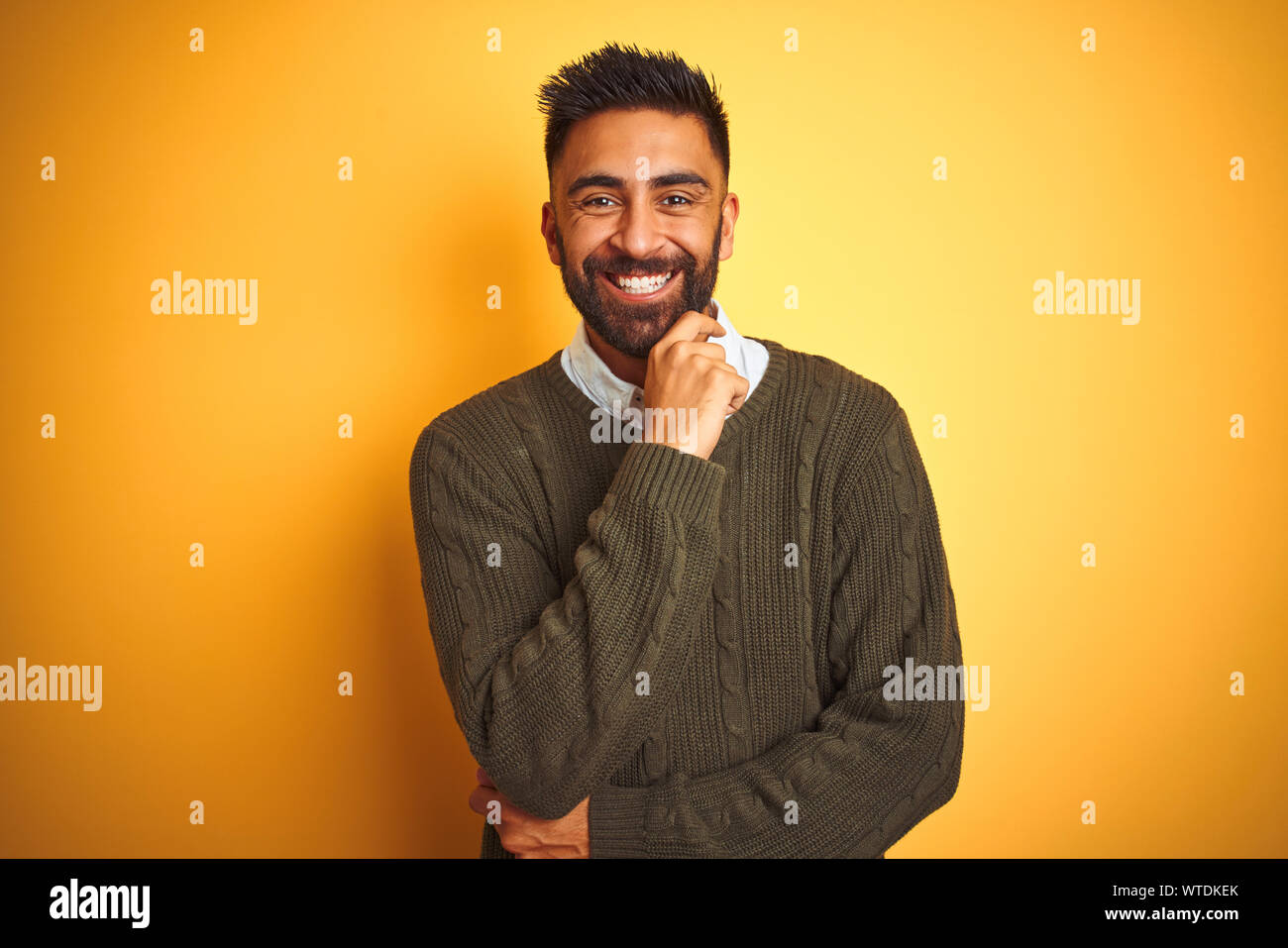 Young indian man wearing green sweater and shirt standing over isolated ...