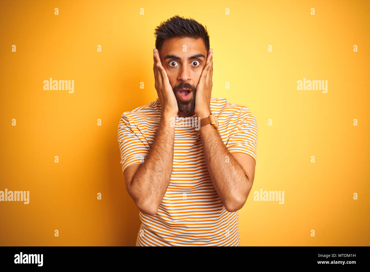 Young indian man wearing t-shirt standing over isolated yellow ...