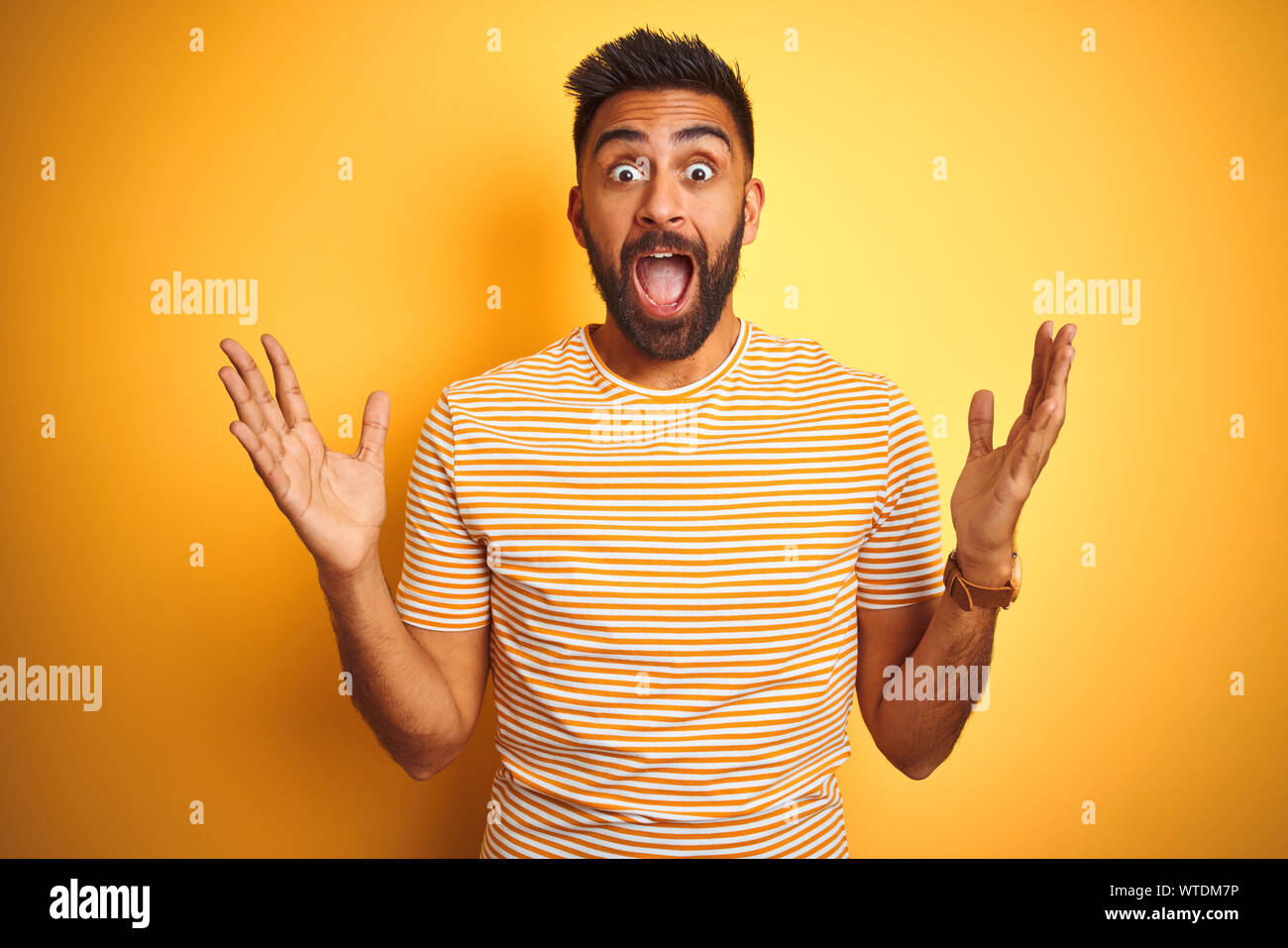 Young indian man wearing t-shirt standing over isolated yellow ...