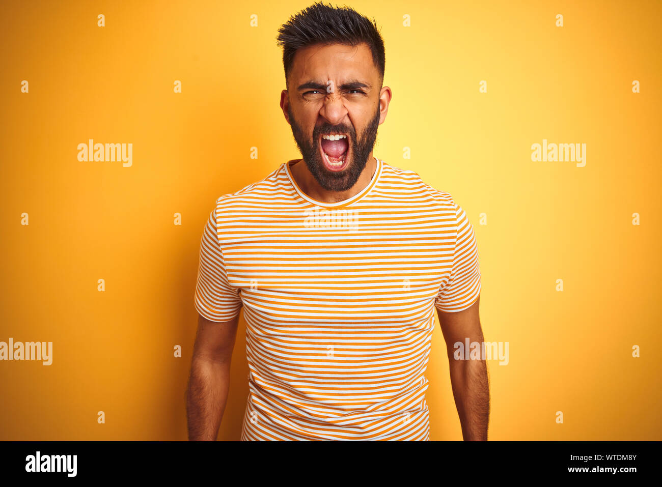 Young indian man wearing t-shirt standing over isolated yellow ...