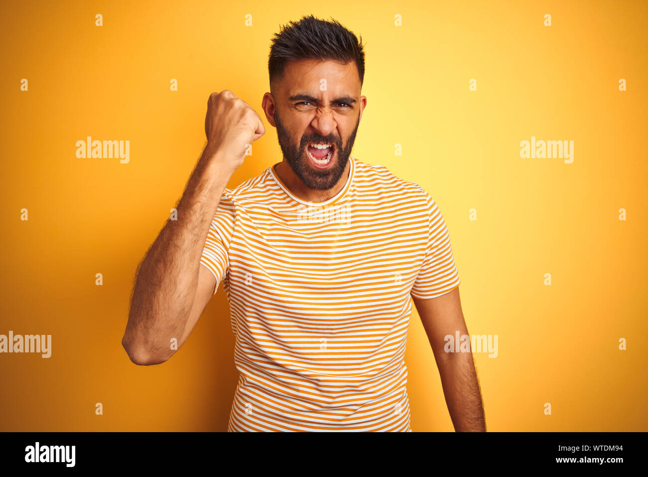 Young indian man wearing t-shirt standing over isolated yellow ...