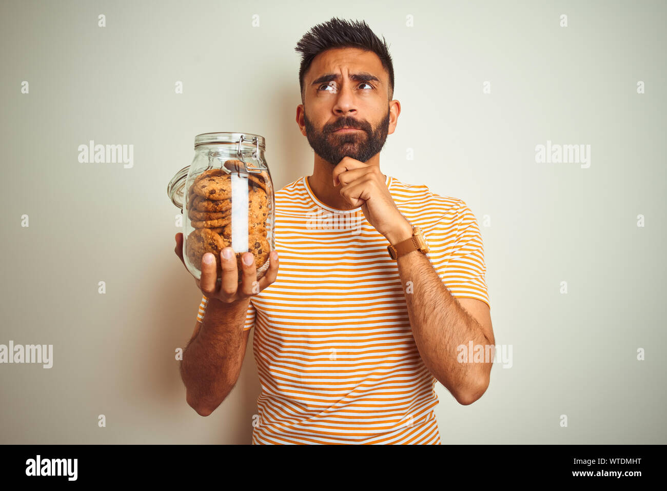 Young indian man holding jar of cookies standing over isolated white ...