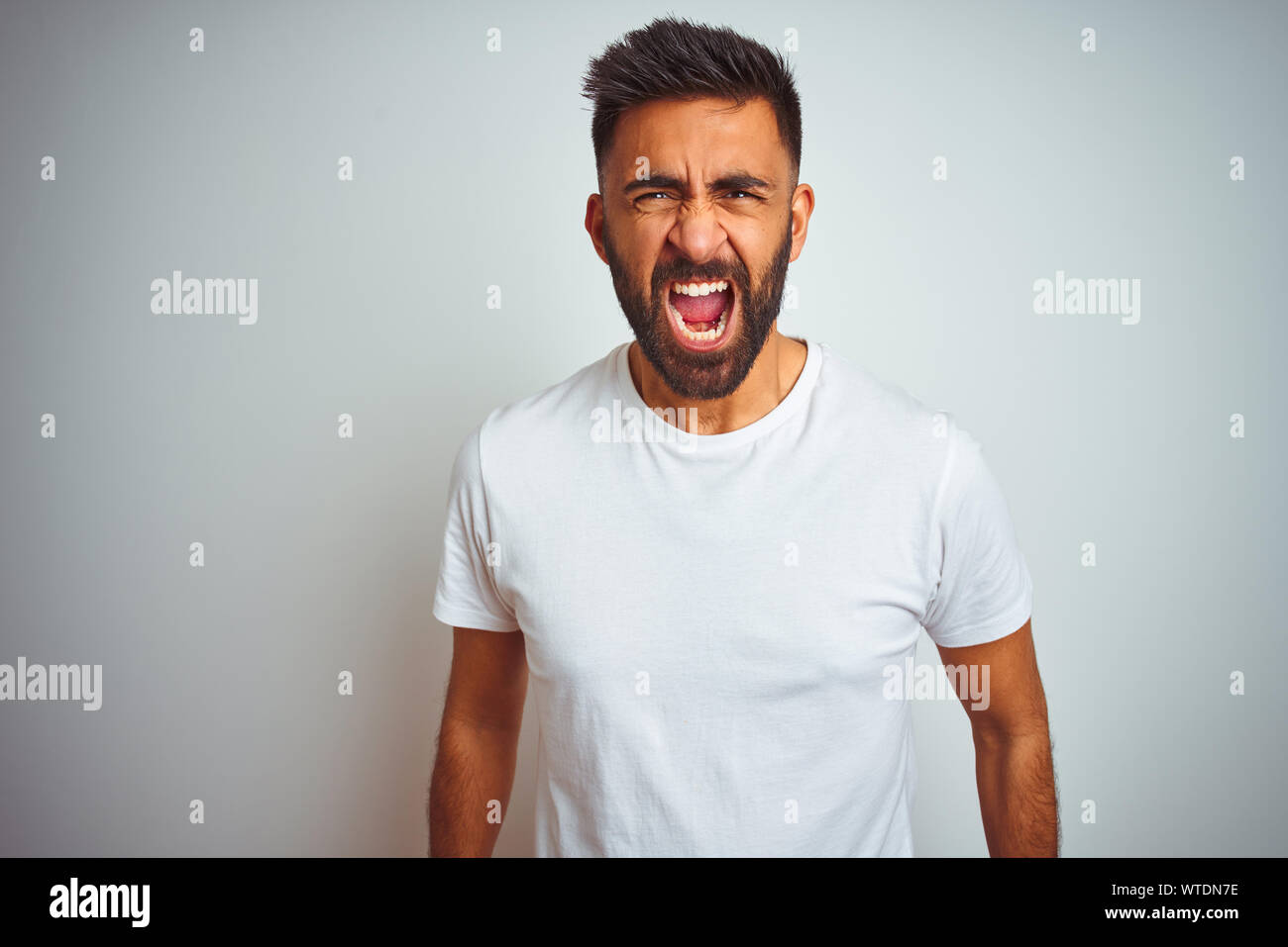 Young indian man wearing t-shirt standing over isolated white ...