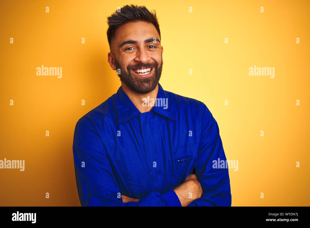 Handsome indian worker man wearing uniform over isolated yellow ...
