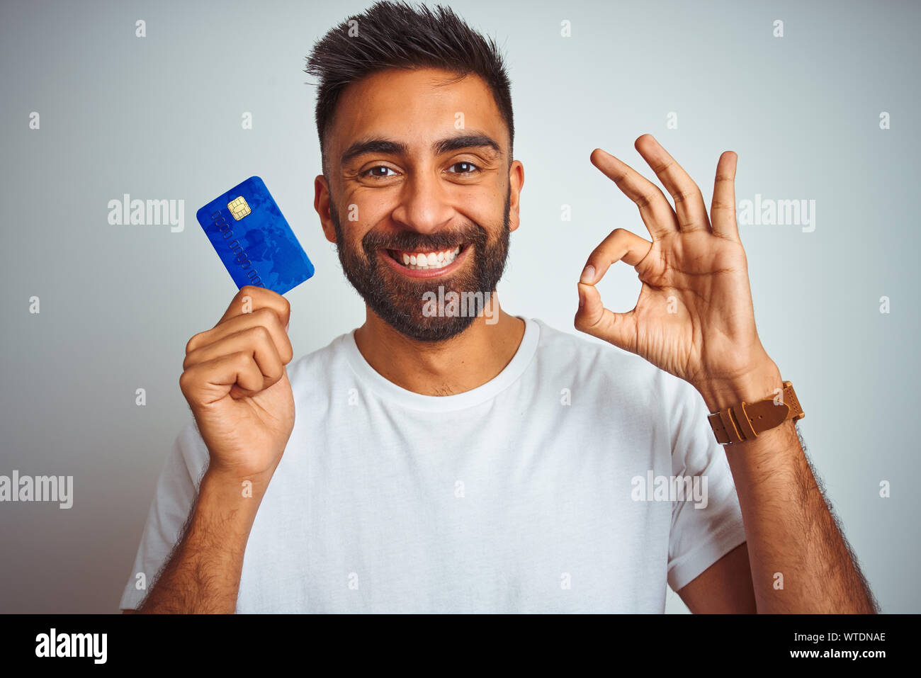 Young indian customer man holding credit card standing over isolated ...