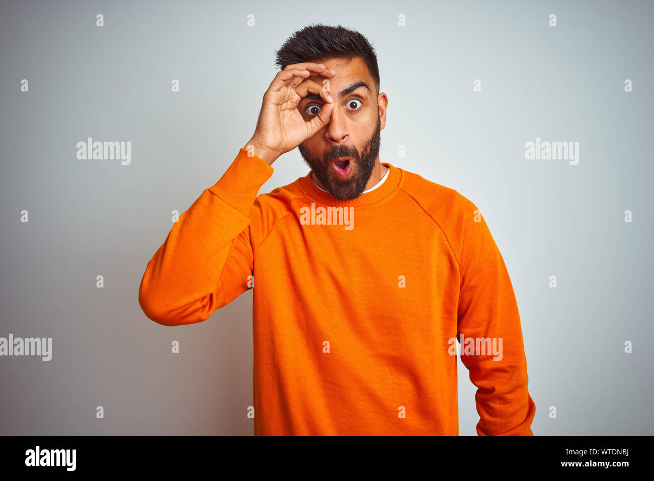 Young indian man wearing orange sweater over isolated white background ...