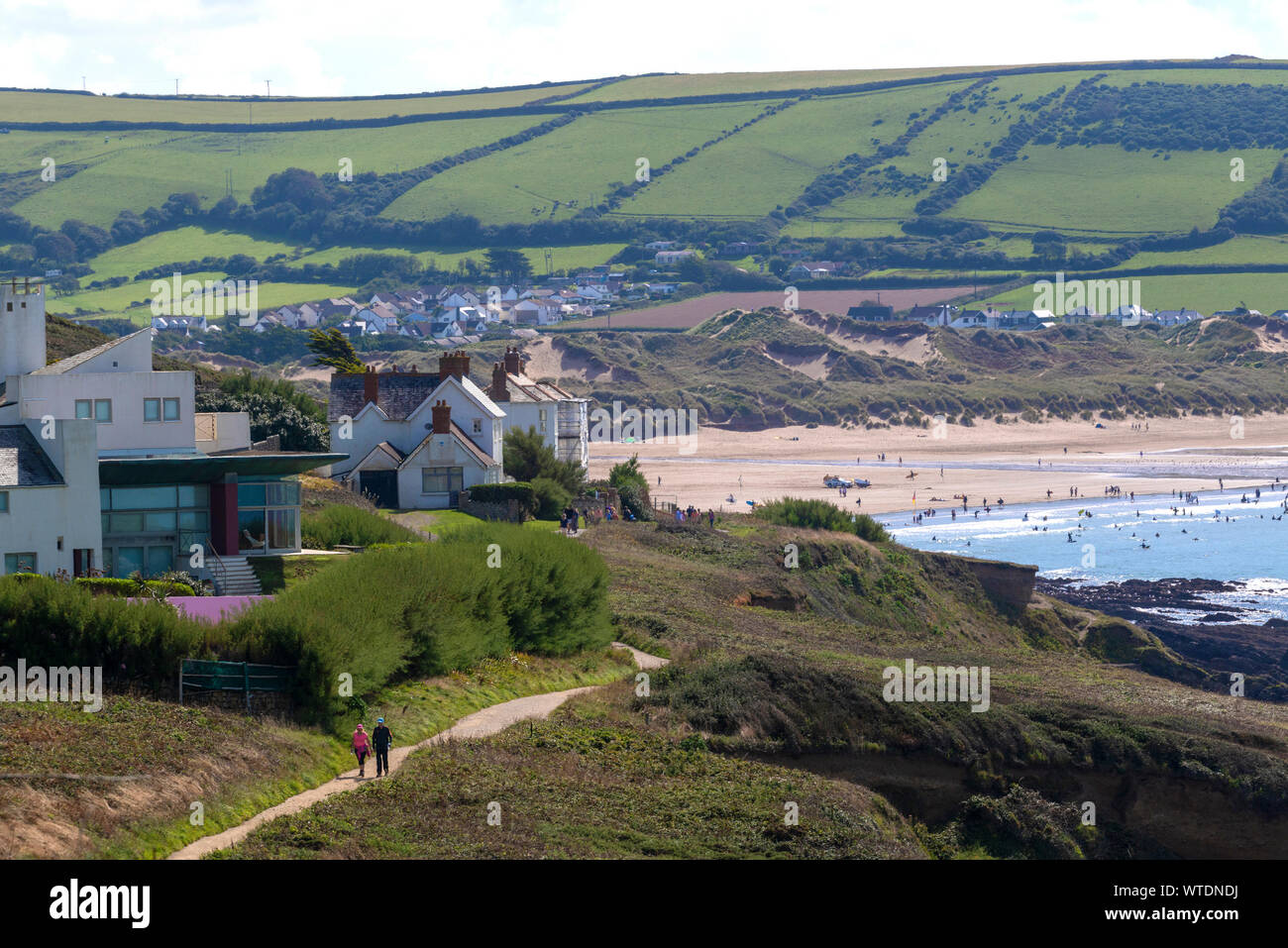 Couple walking along footpath above Croyde Bay and the surfing beach and seaside town of Croyde ...