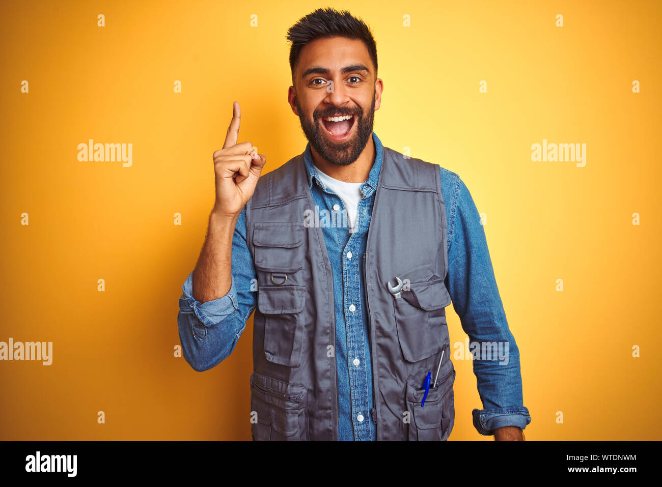 Handsome indian technician man wearing uniform over isolated yellow ...