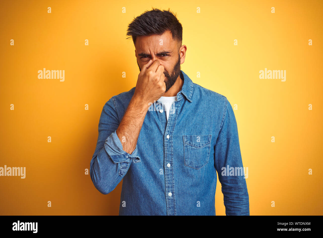 Young indian man wearing denim shirt standing over isolated yellow ...