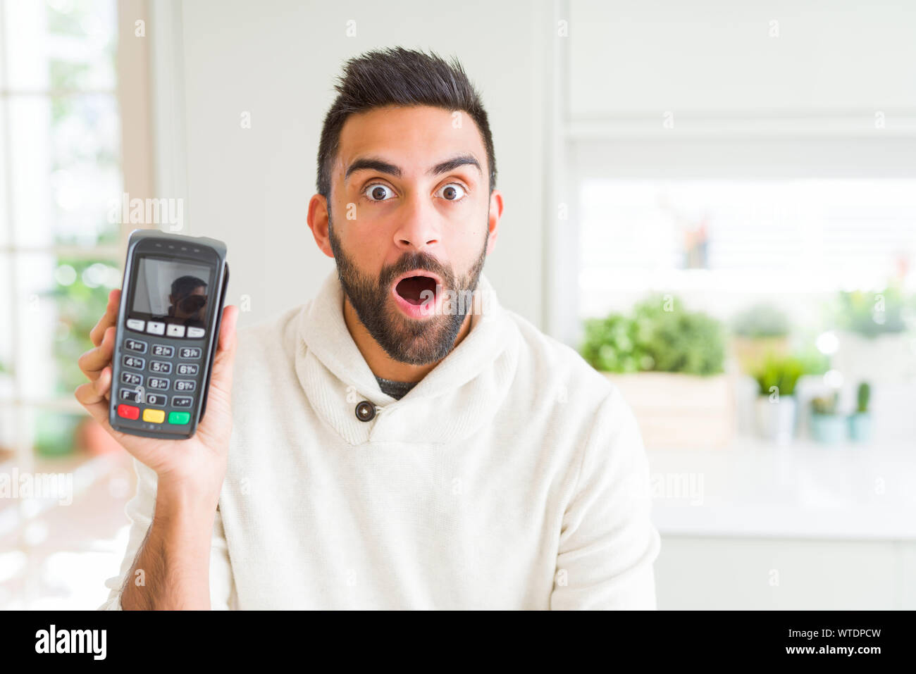 Handsome hispanic man holding point of sale terminal dataphone scared ...