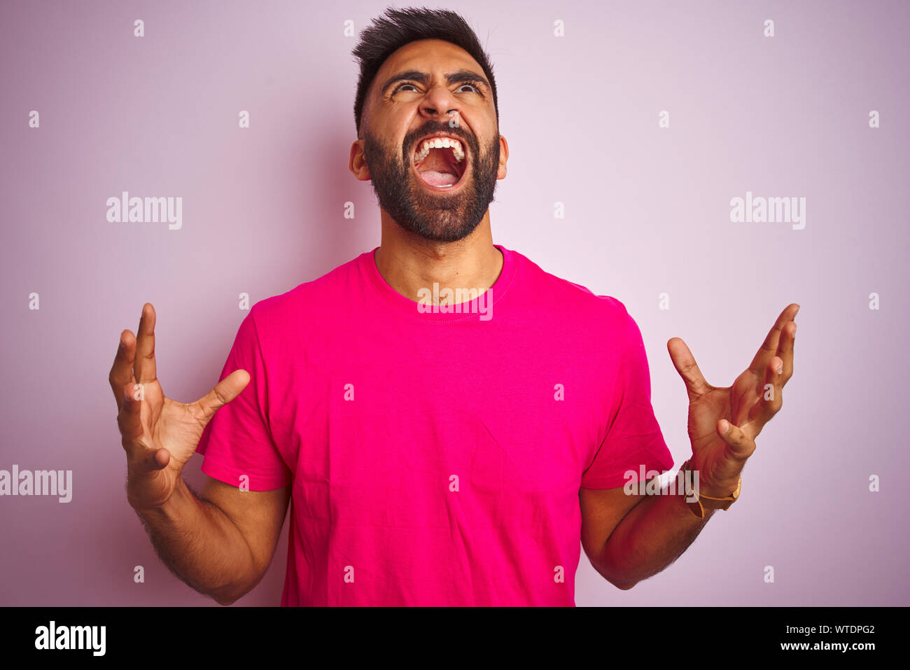 Young indian man wearing t-shirt standing over isolated pink background ...