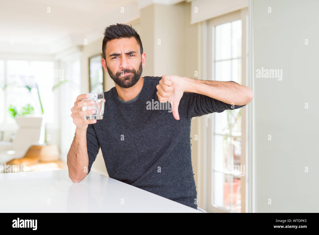 Handsome hispanic man drinking a fresh glass of water with angry face ...