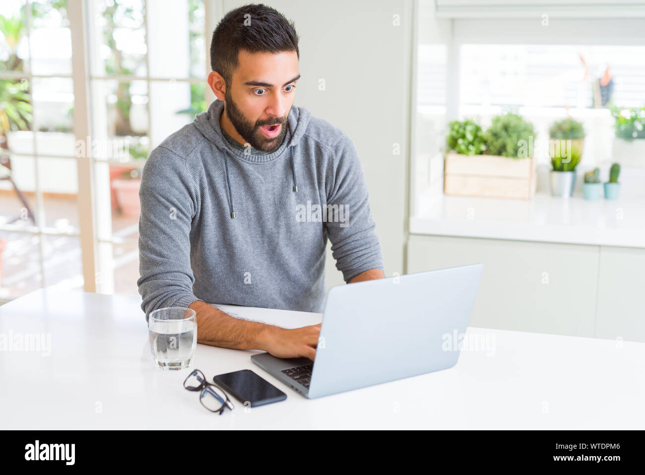 Handsome hispanic man working using computer laptop scared in shock ...