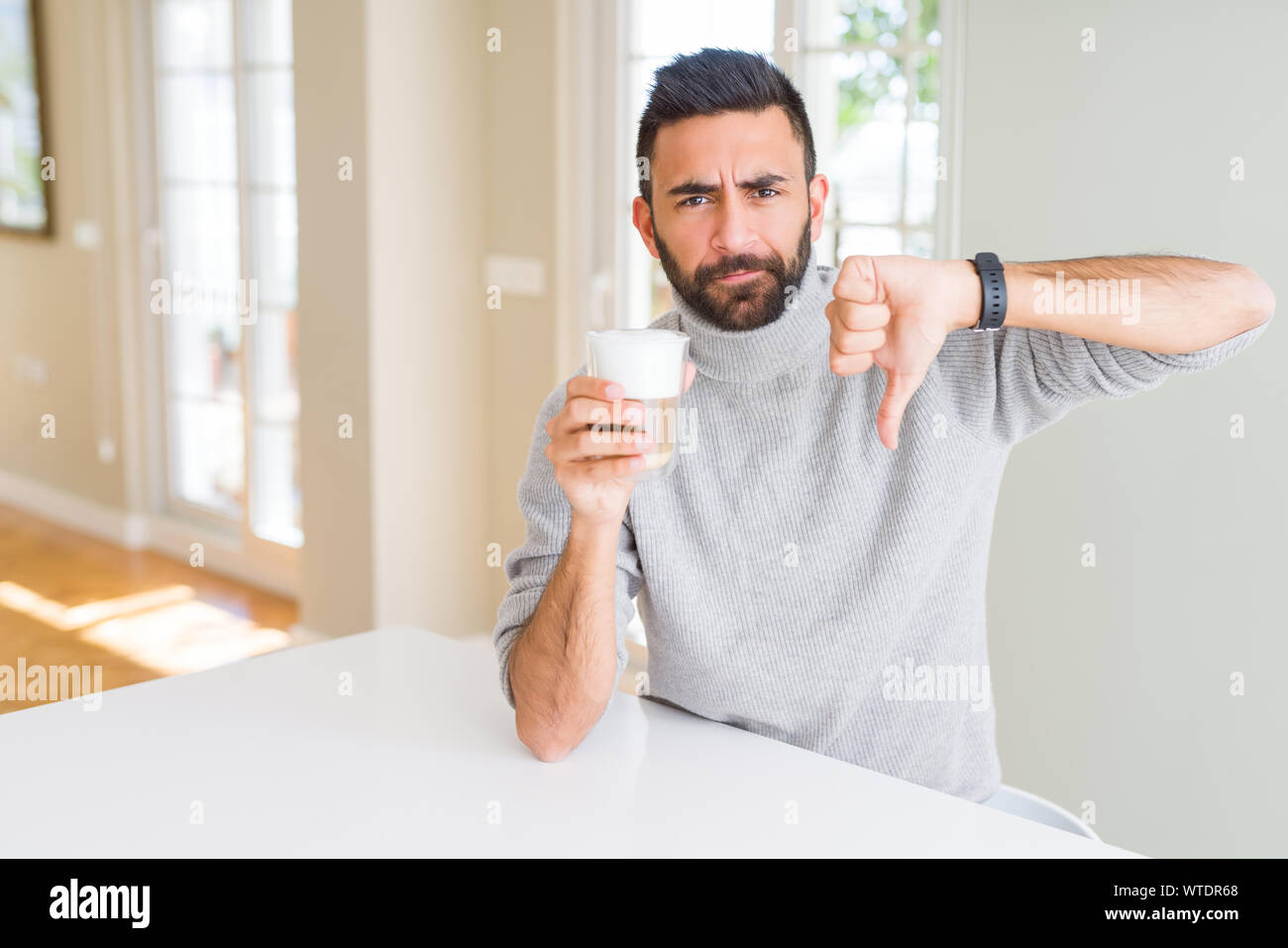 Handsome hispanic man drinking a cup of coffee with angry face ...