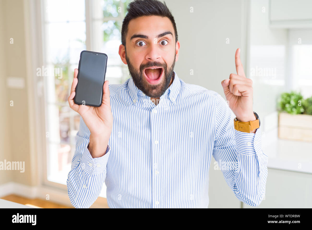 Handsome hispanic business man showing smartphone screen surprised with ... Handsome hispanic business man showing smartphone screen surprised with ...