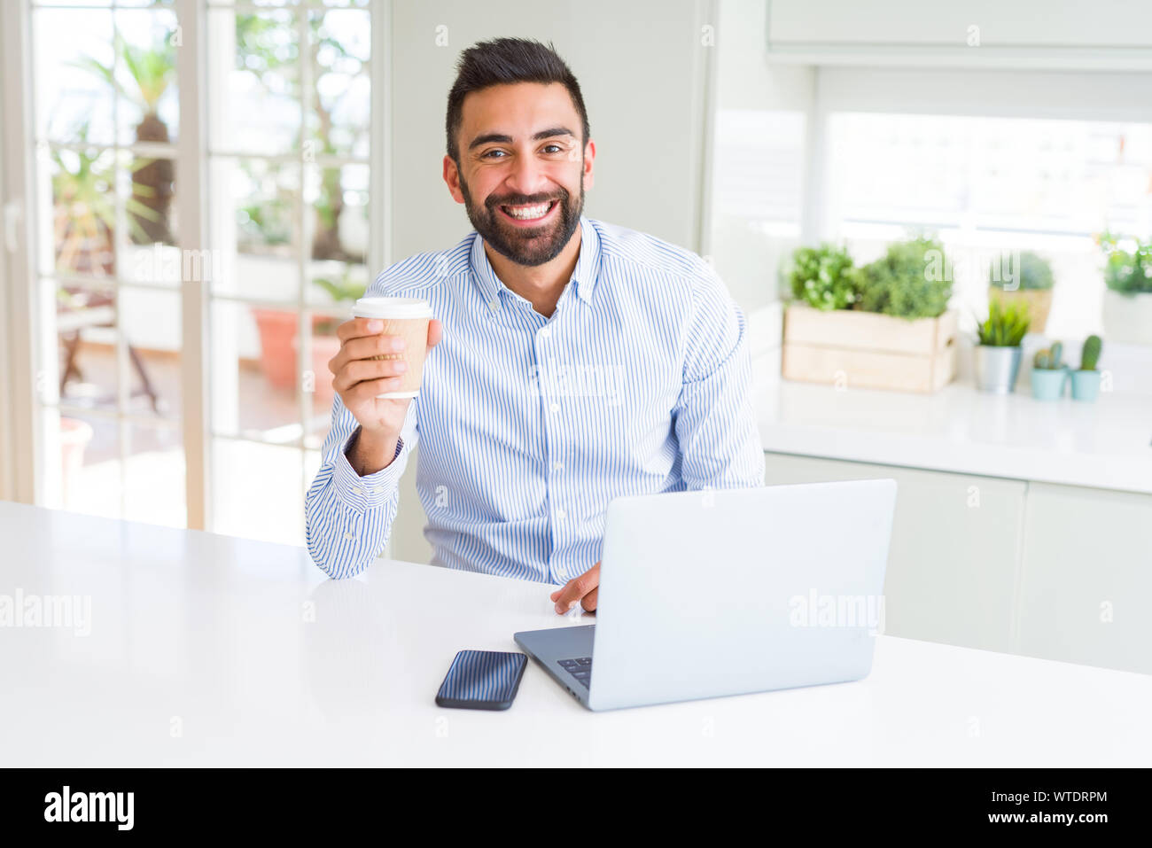 Handsome hispanic man working using computer laptop and drinking a cup ...