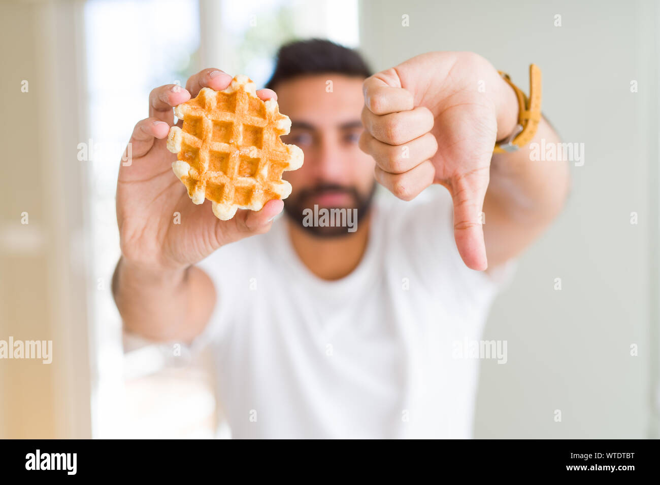 Handsome hispanic man eating sweet belgian waffle pastry with angry ...