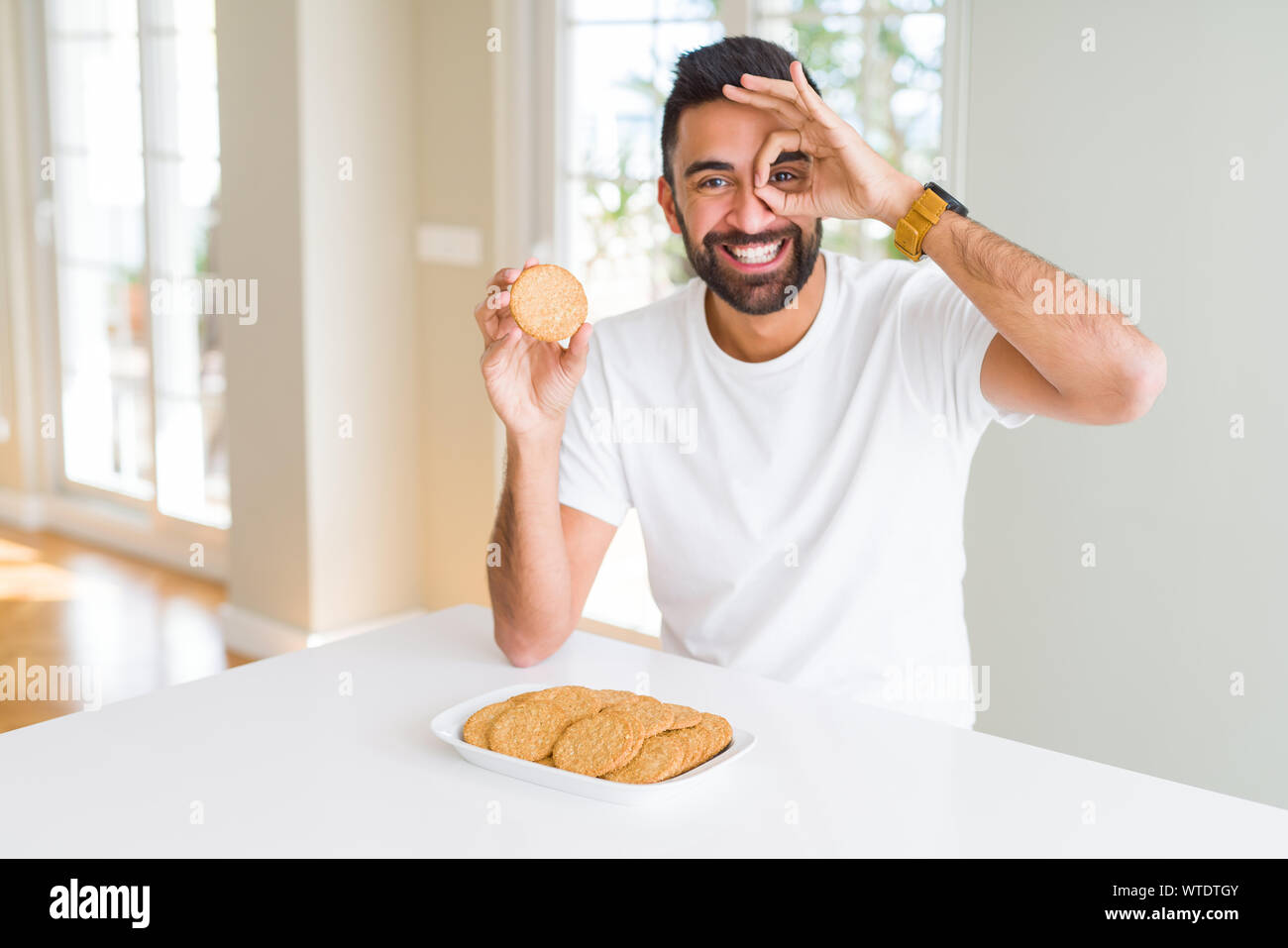 Handsome hispanic man eating healthy whole grain biscuits with happy ...