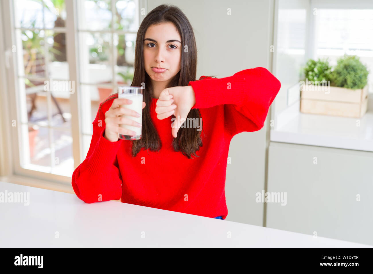 Beautiful young woman drinking a glass of fresh milk with angry face ...