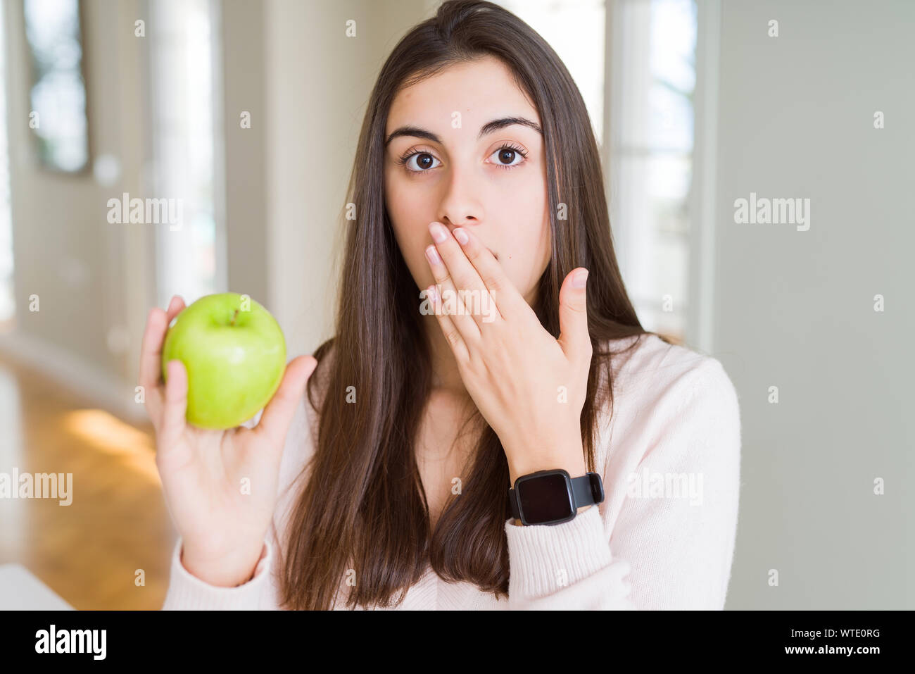 Beautiful young woman eating healthy green apple fruit cover mouth with ...