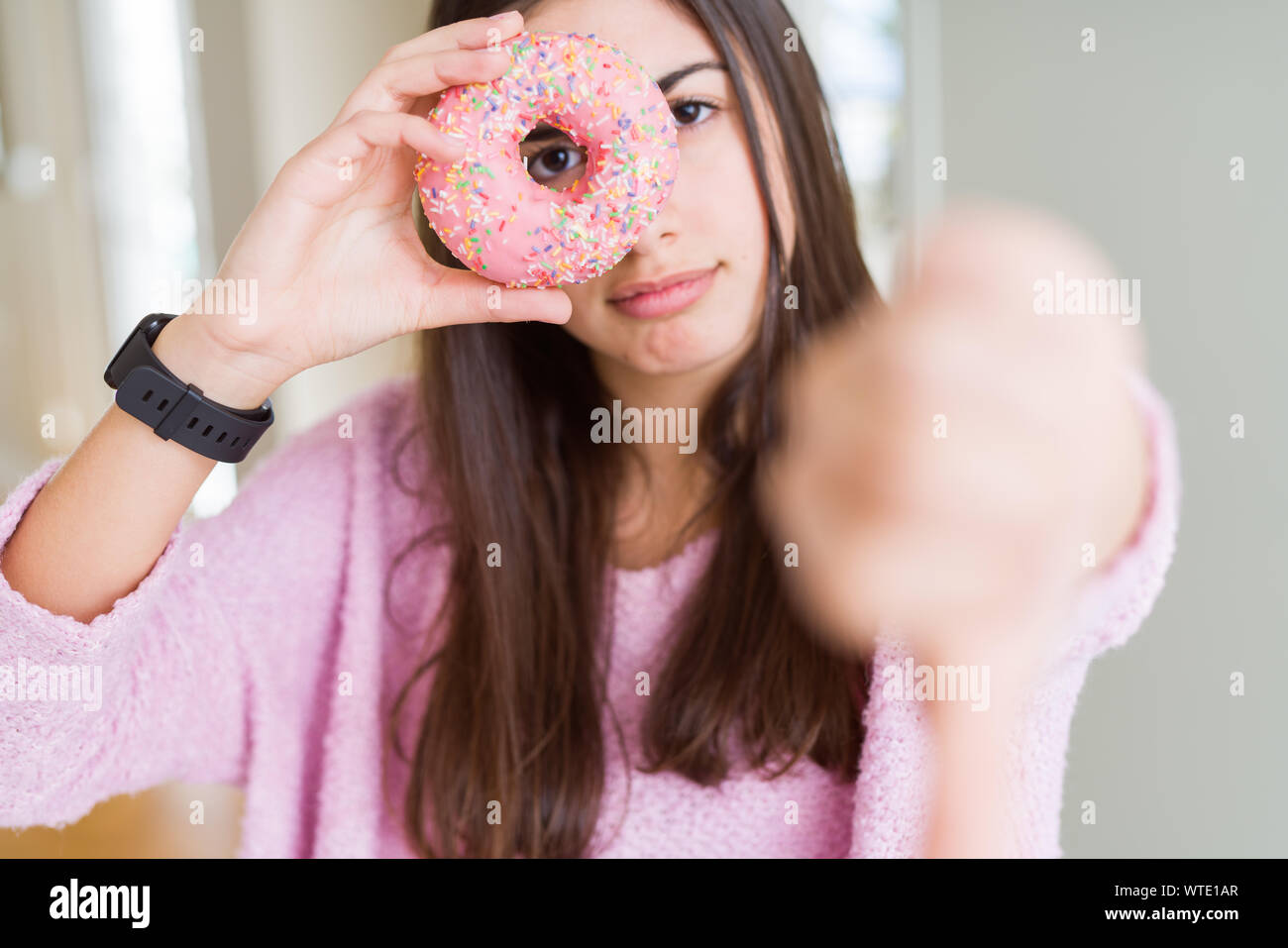 Beautiful young woman eating pink chocolate chips donut with angry face ...