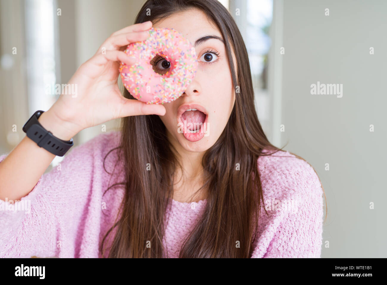 Beautiful young woman eating pink chocolate chips donut scared in shock ...