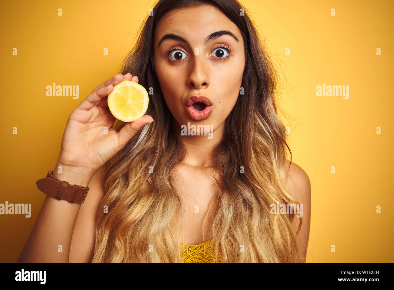 Young beautiful woman holding half lemon over yellow isolated ...