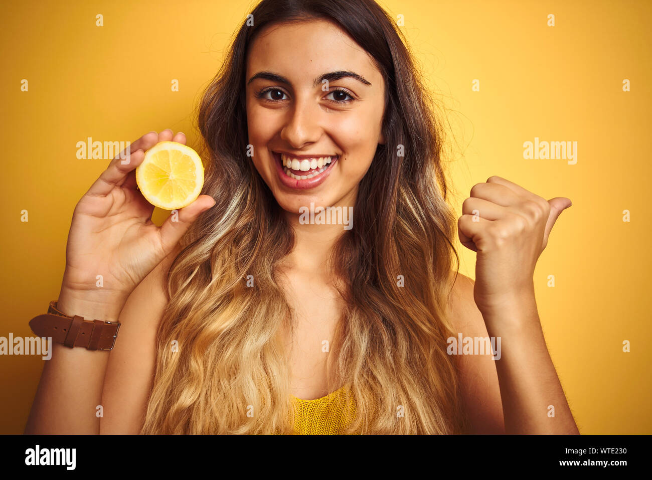 Young beautiful woman holding half lemon over yellow isolated ...