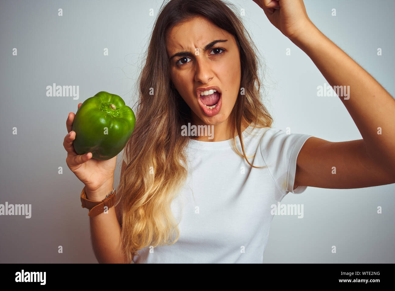 Young beautiful woman holding green pepper over white isolated ...