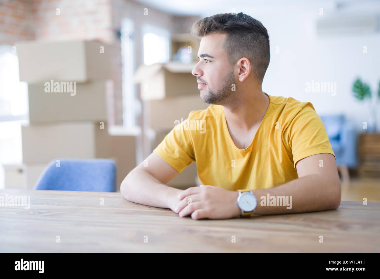 Young man sitting on the table with cardboard boxes behind him moving ...